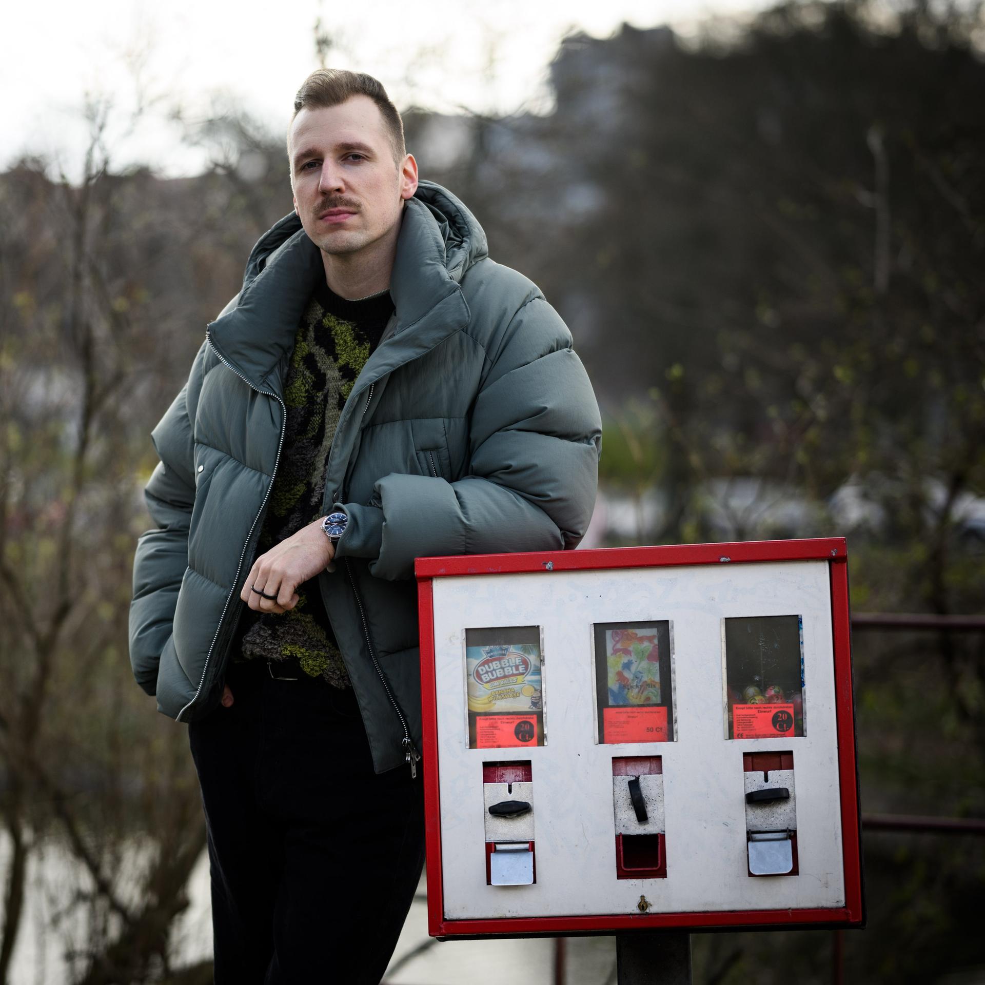 Lukas Strobel, besser bekannt als der Rapper Alligatoah, steht neben einem Kaugummiautomat.