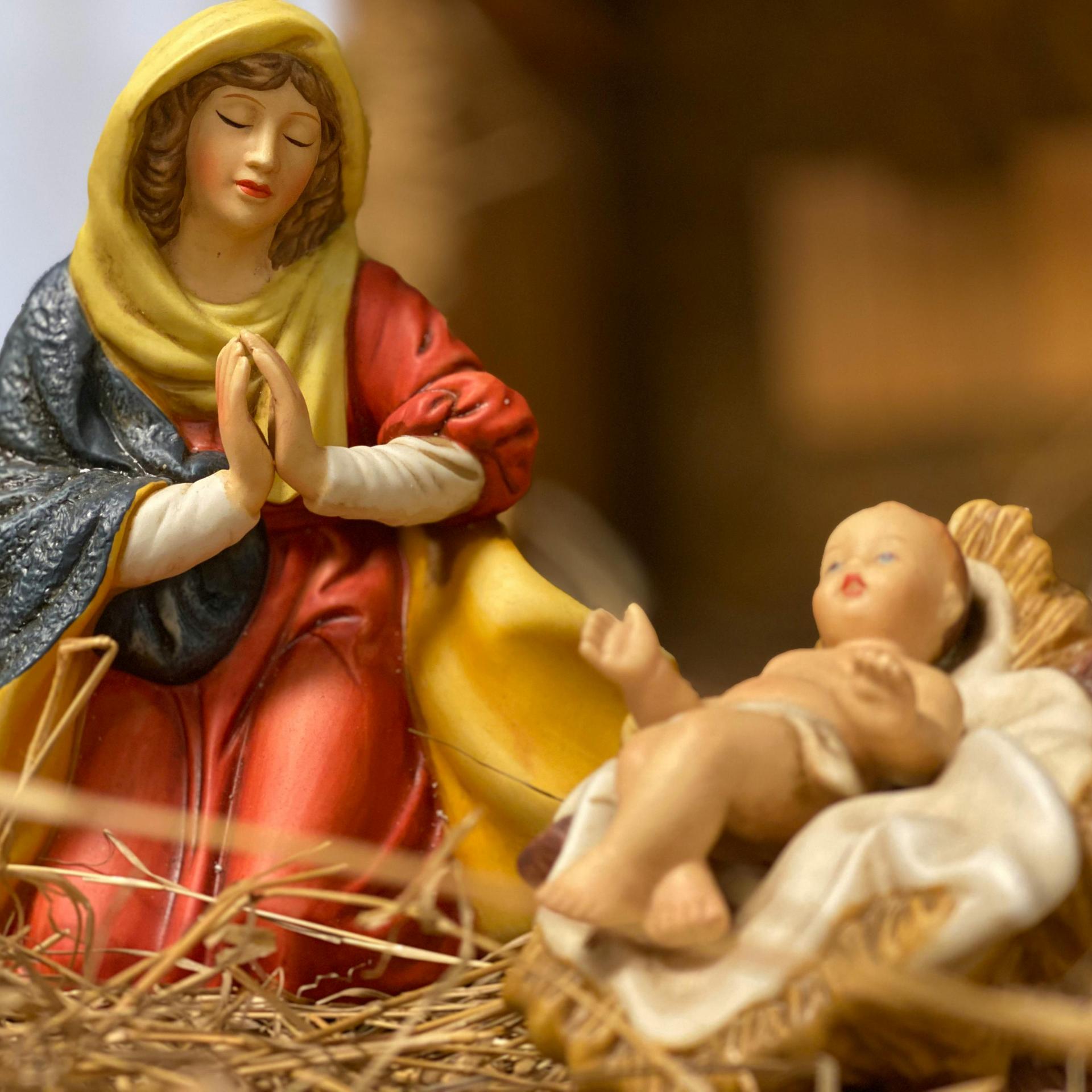 Blick auf eine Krippe, in der Maria betend neben einem Krippenkind kniet.